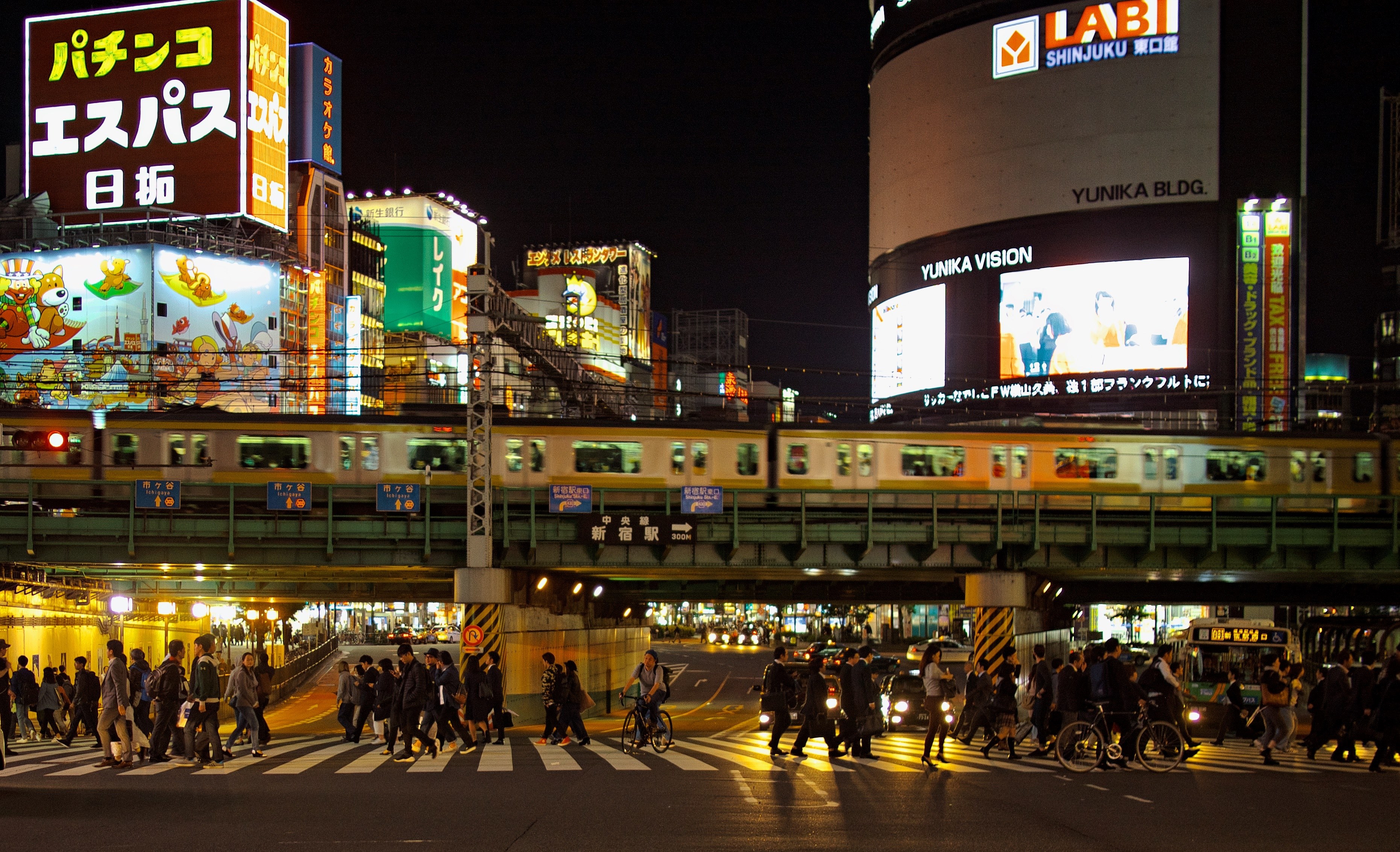 pedestrians walk as a train tram passes overhead in shinjuku, busy ...