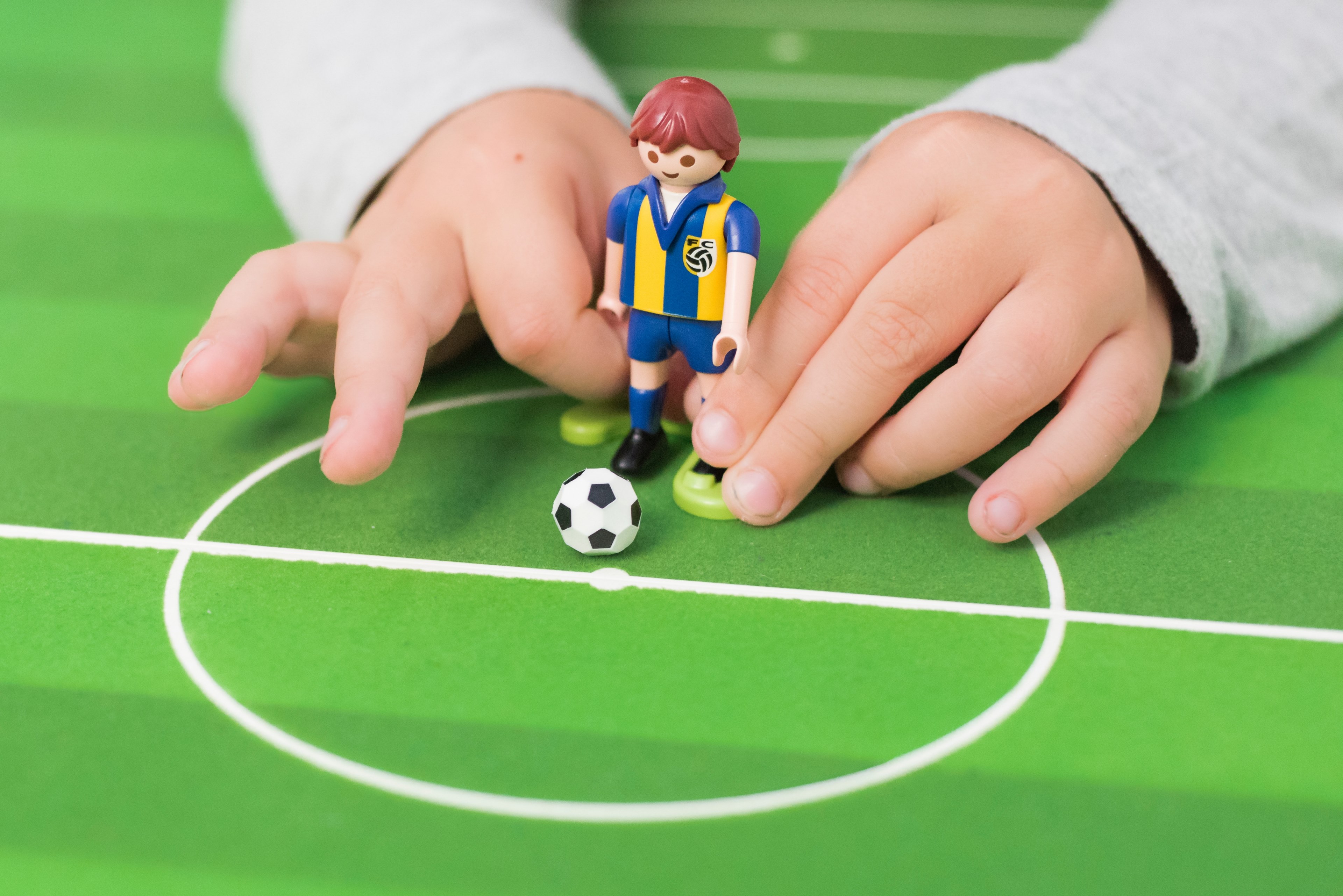 a child plays with a soccer figure on a green table, the pleasure of ...