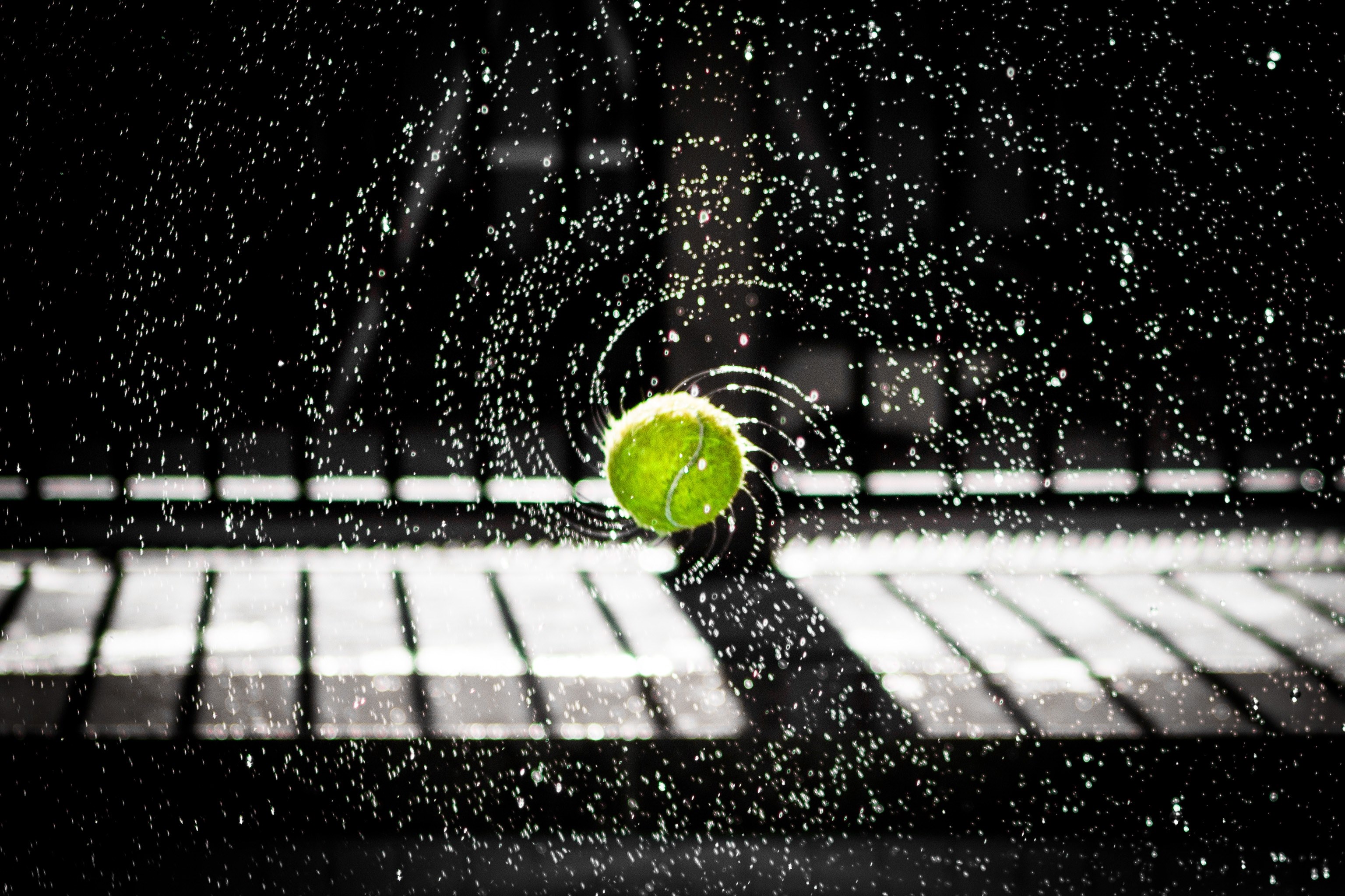 wet tennis ball spinning with the water spraying off, flying through ...