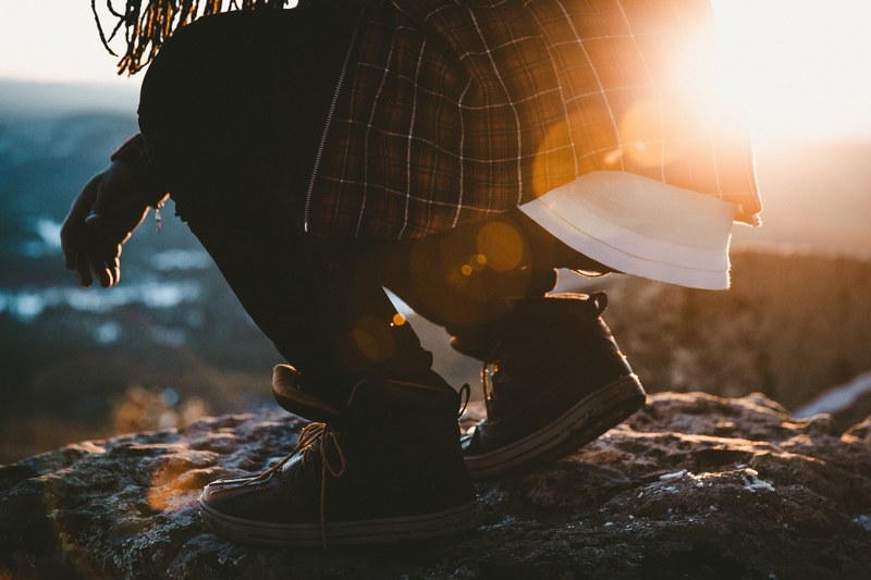 person with dreadlocks in boots and plaid crouching down on the rocks ...