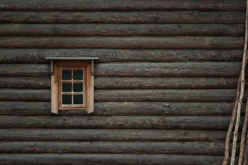 the wall of a log cabin with a small wooden window to the left and some ...